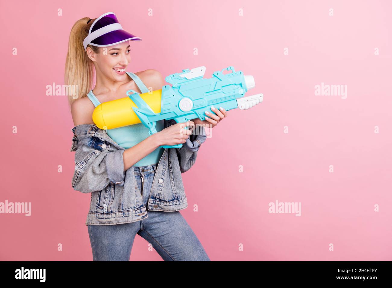 Portrait of attractive cheerful girl using childish water gun shooting ...
