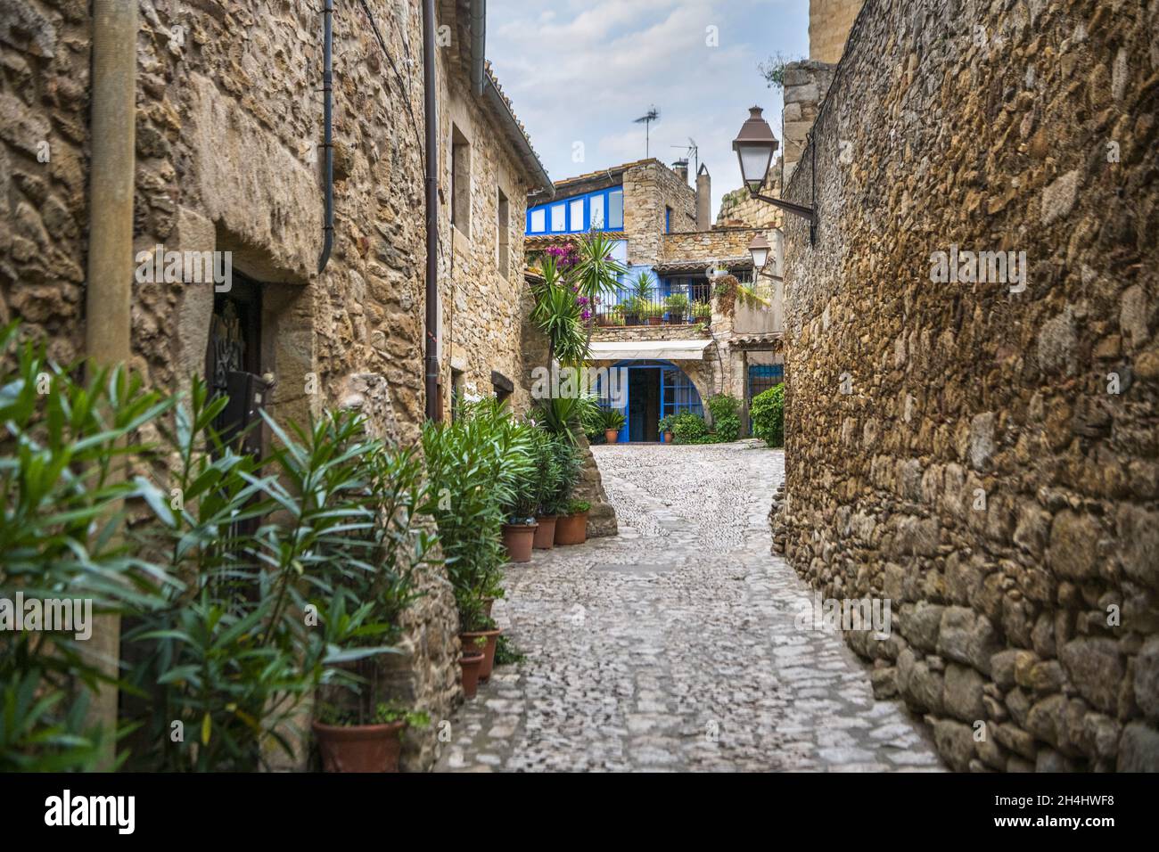 Empty narrow alley with potted plants between old rough weathered stone ...
