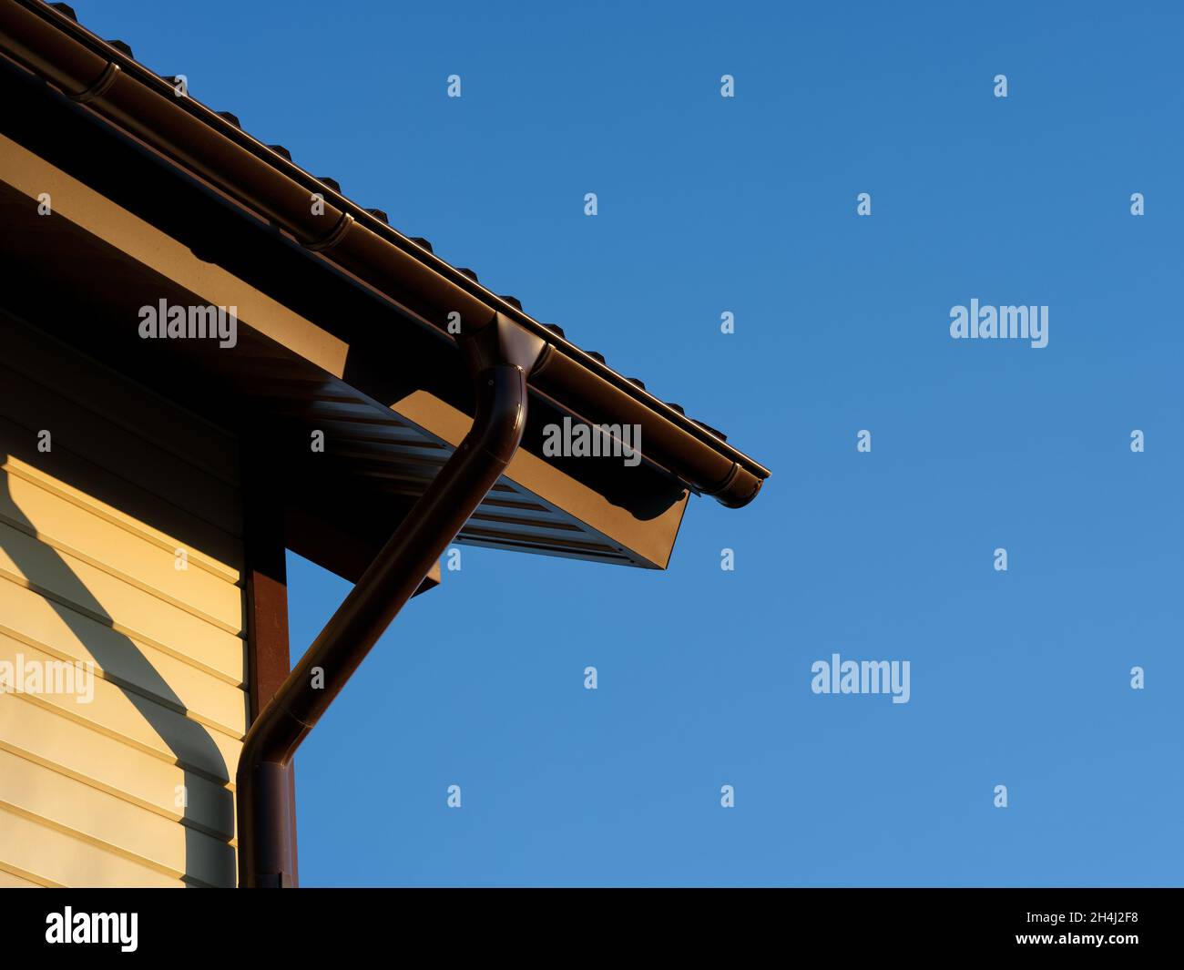 A roof with a gutter on a house against a blue sky background. Close-up ...