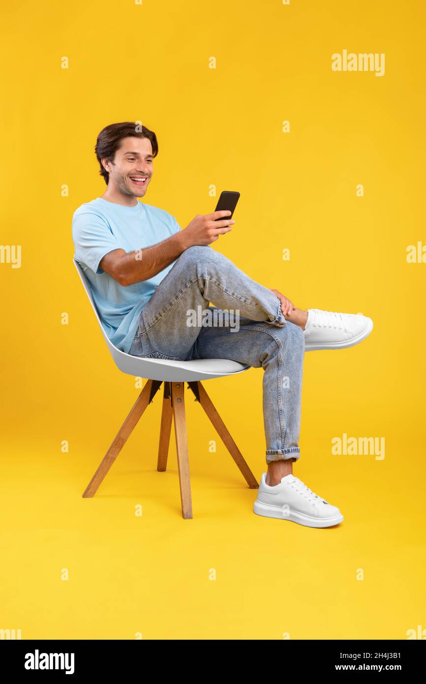 Happy guy using cell phone at studio, sitting on chair Stock Photo - Alamy