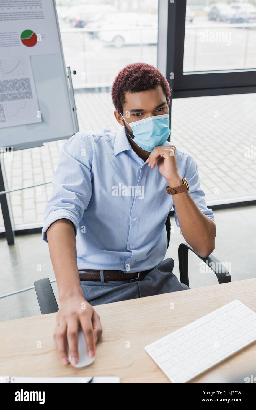 African american manager in medical mask using computer mouse near flip ...
