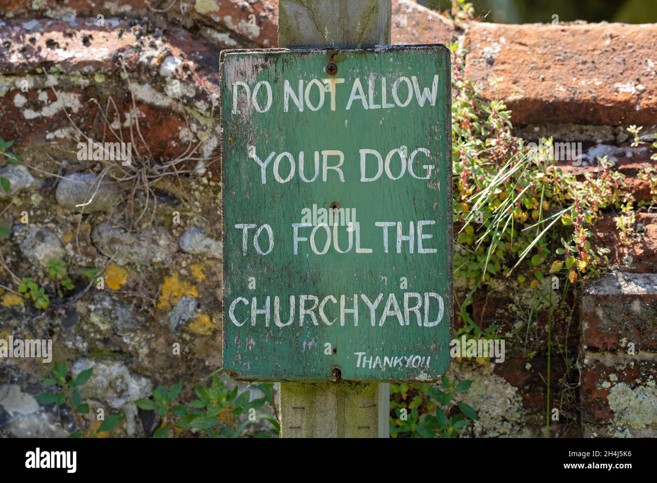 Hand painted sign by a churchyard brick and flintstone wall, DO NOT ...
