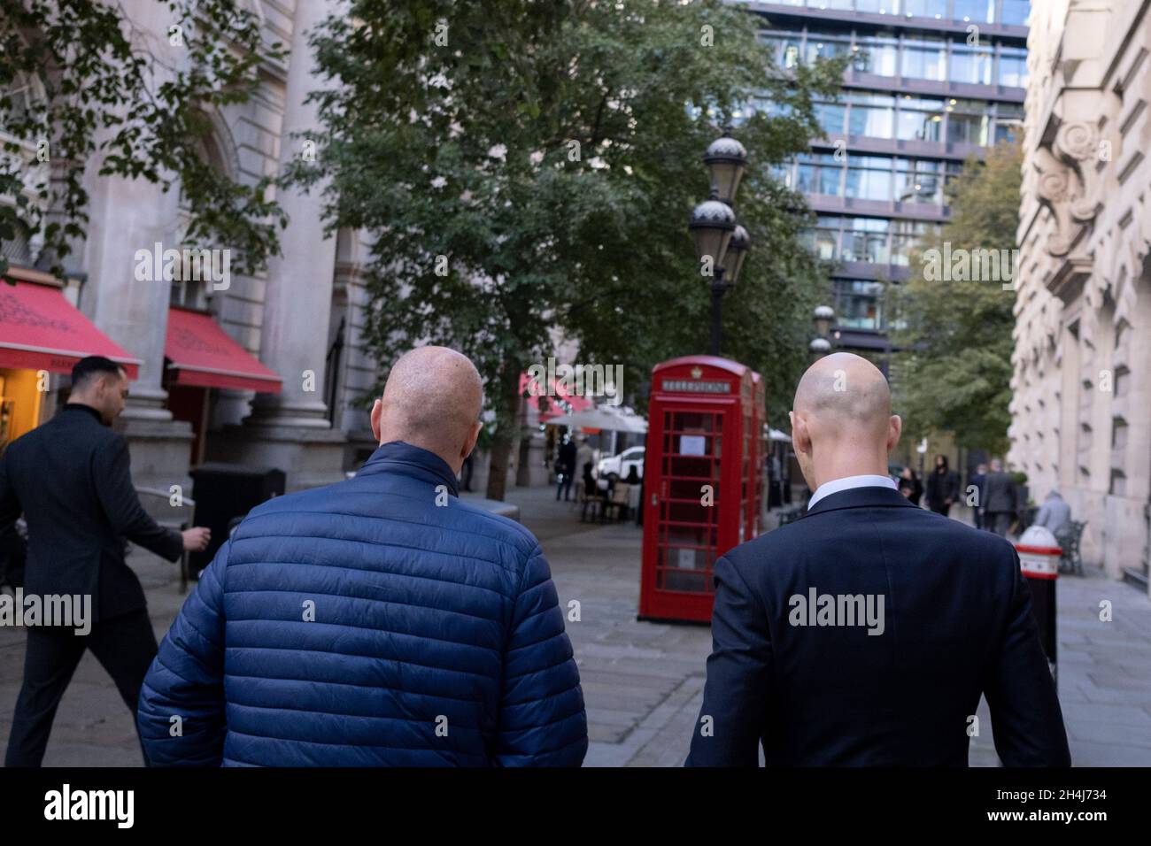 Two businessmen who have shaved, bald heads are seen from the rear as ...