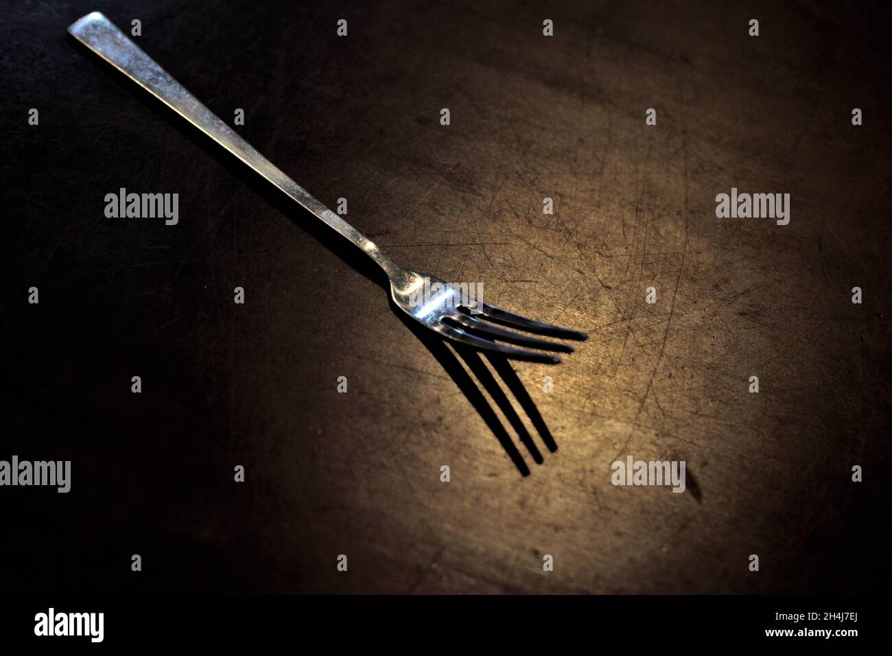 Single fork lying alone on table under spotlight Stock Photo - Alamy