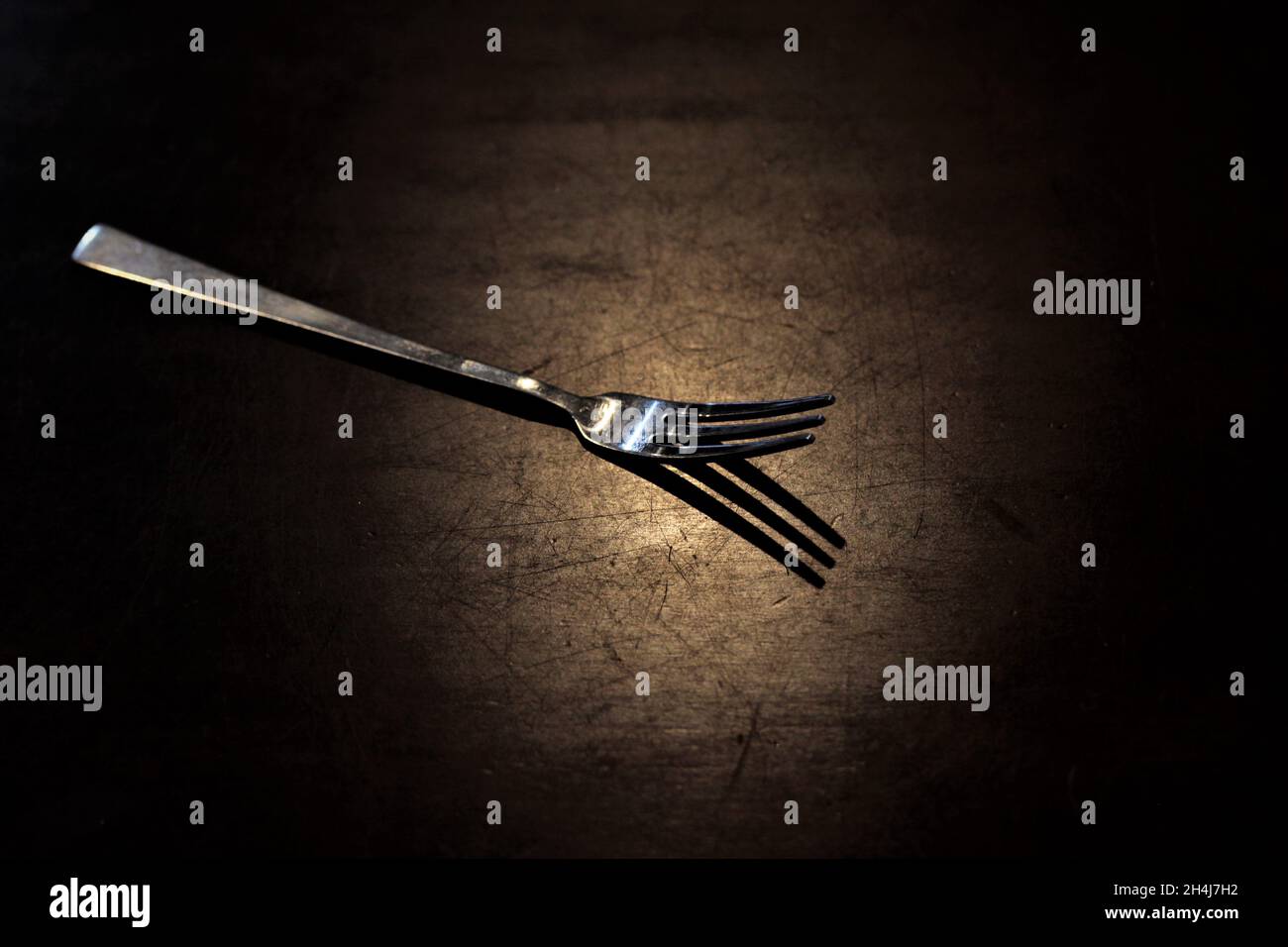 Single fork lying alone on a table under spotlight Stock Photo - Alamy