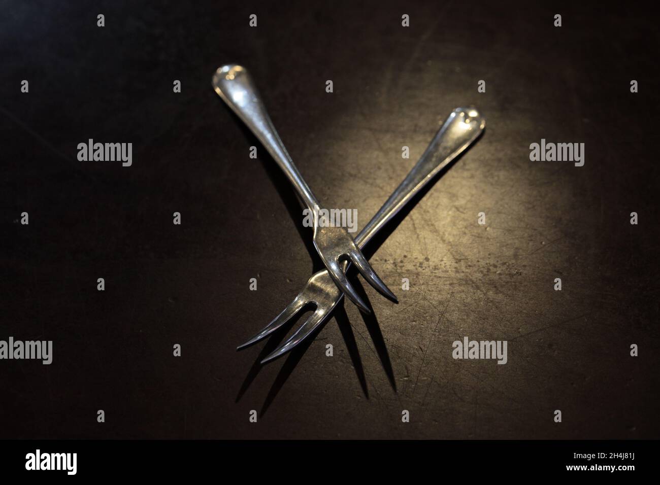 Two forks on a table with strong lighting and shadows create an ...