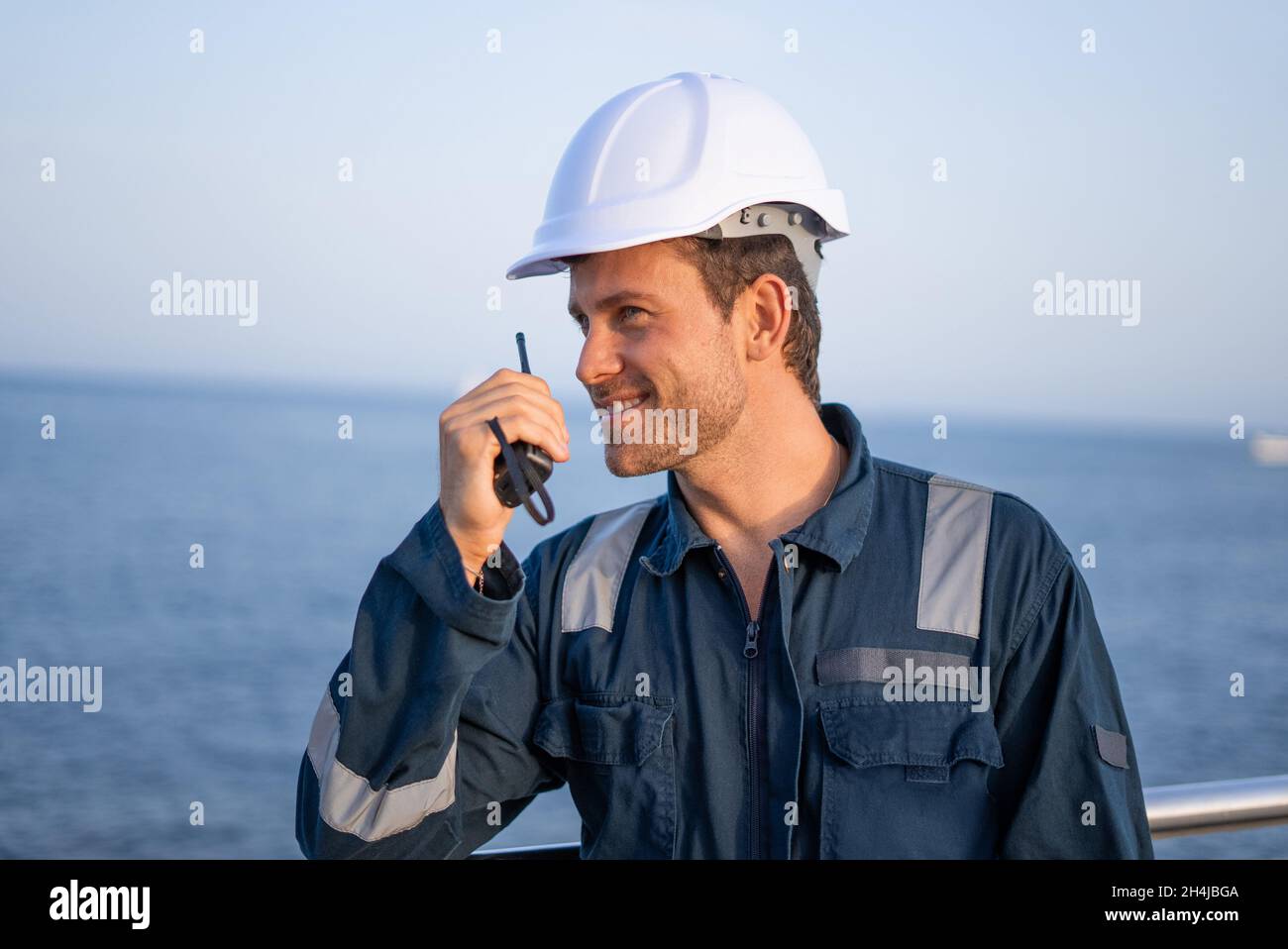 Cheerful young workman in protective uniform and hardhat speaking on ...
