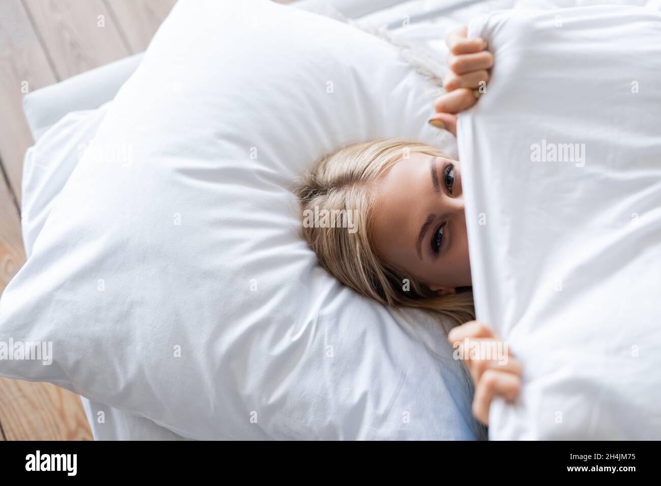 top view of young woman covering face with blanket while lying on bed ...