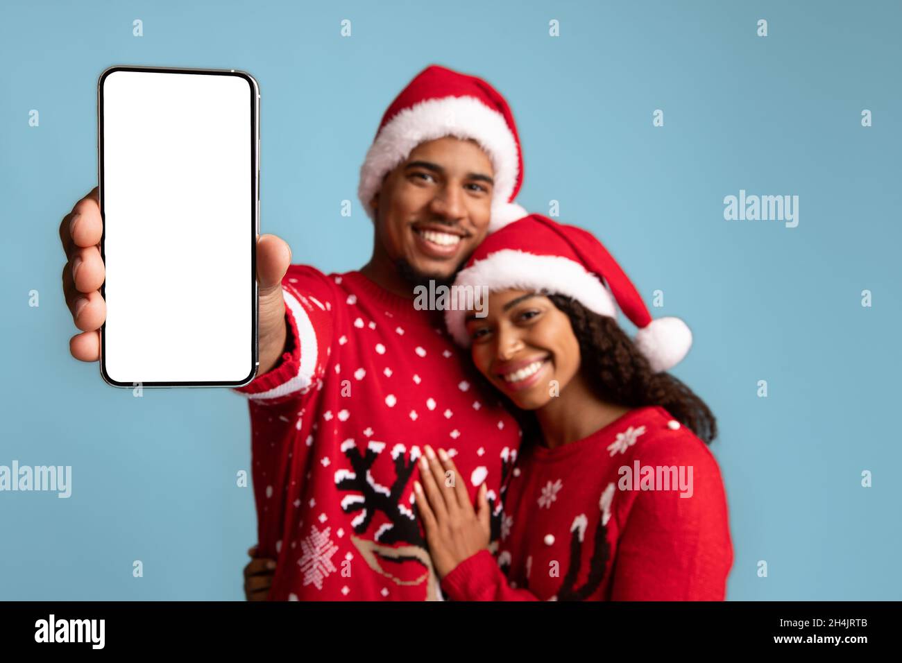 Loving millennial black couple celebrating xmas together, embracing and showing modern cellphone ...