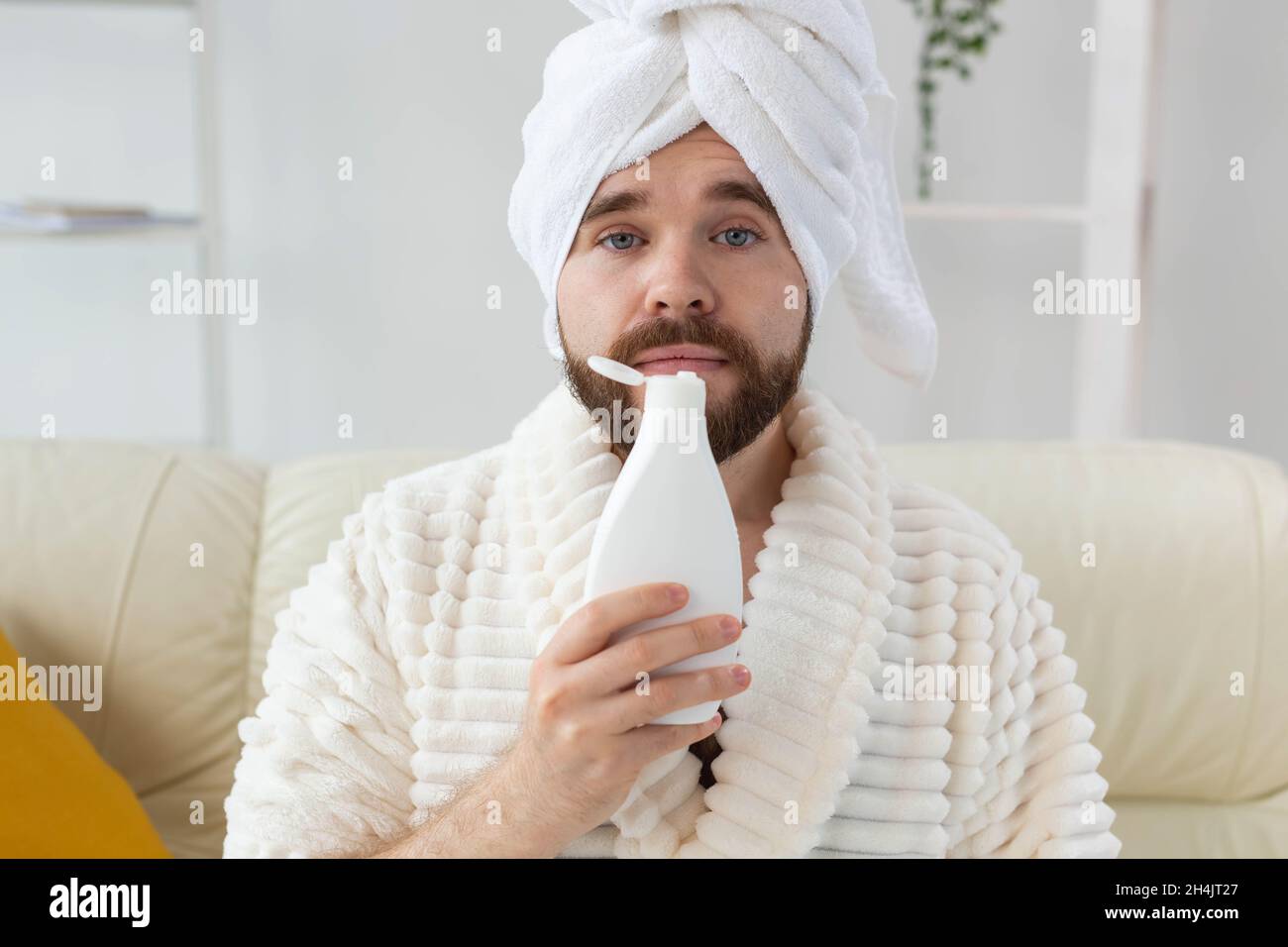 Bearded male with towel on his head applying body lotion cream. Guy ...