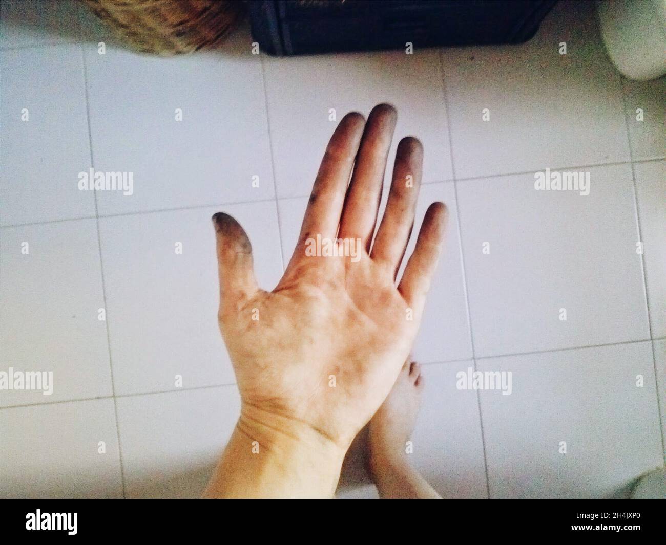 Overhead view of a barefoot person with oil stained hands standing in a ...