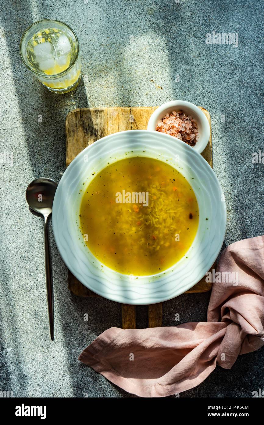 Bowl of chicken broth with spaghetti and a glass of iced lemon water ...