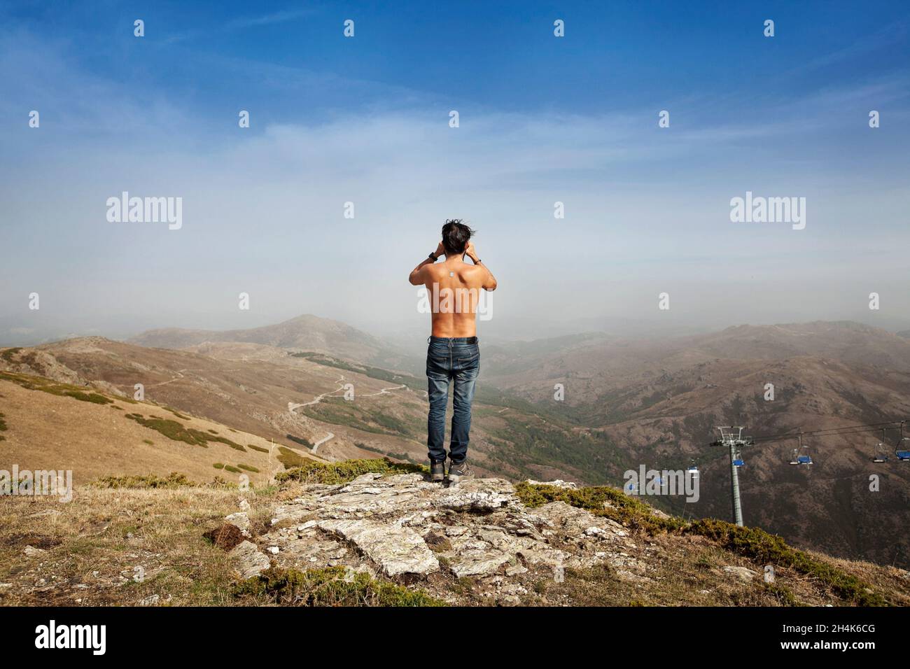 A young man, seen from behind, stands on the top of a mountain to look ...