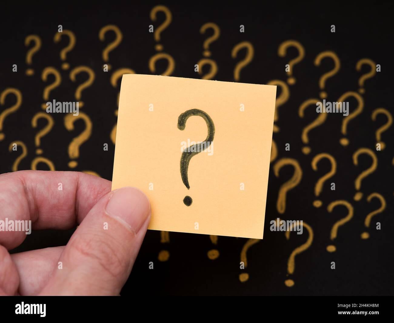 A man holding a sticky note with a question mark on it in his hand ...