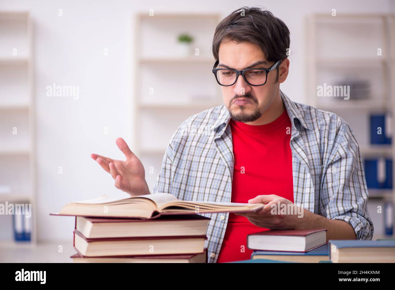 Young student and too many books in the classroom Stock Photo - Alamy