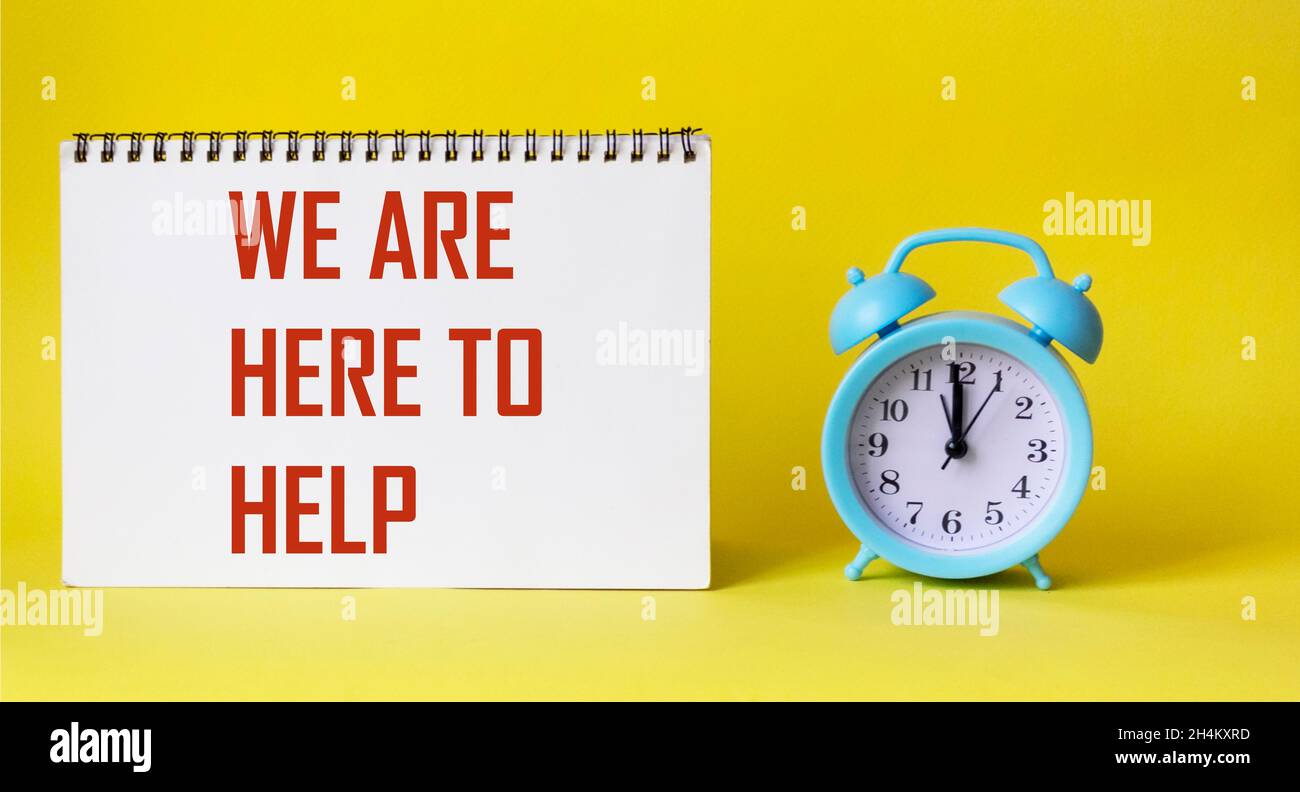 We are here to help written on a notepad, next to an alarm clock on a ...