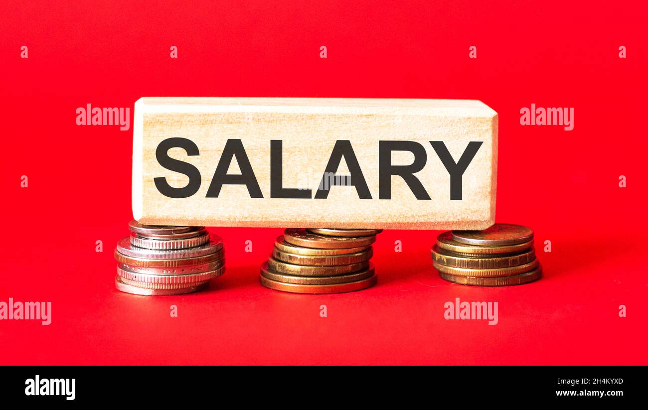 Salary text written on a wooden block with folded coins on a red ...