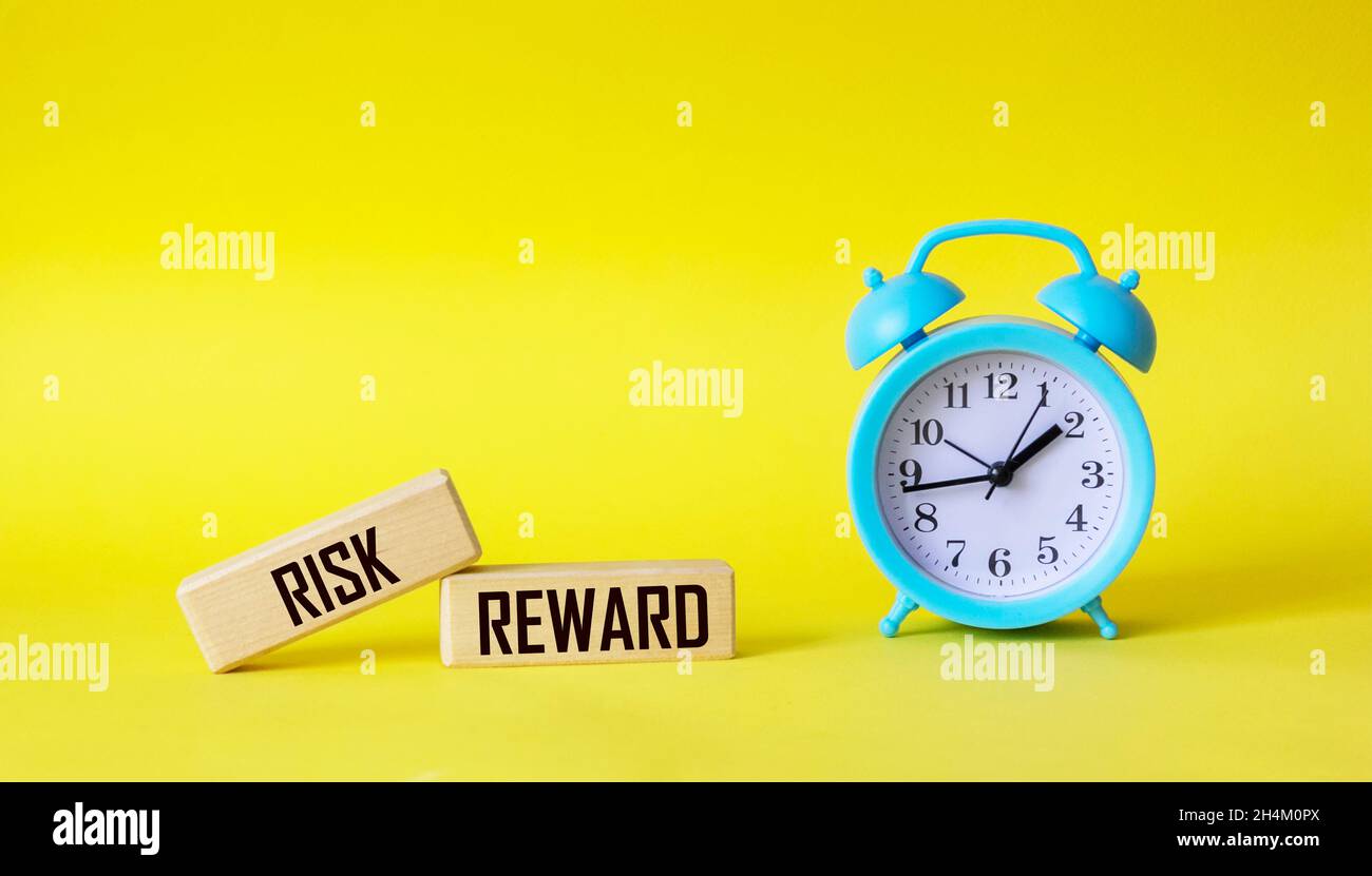 Risk, reward - phrase on wooden blocks and yellow background with clock ...