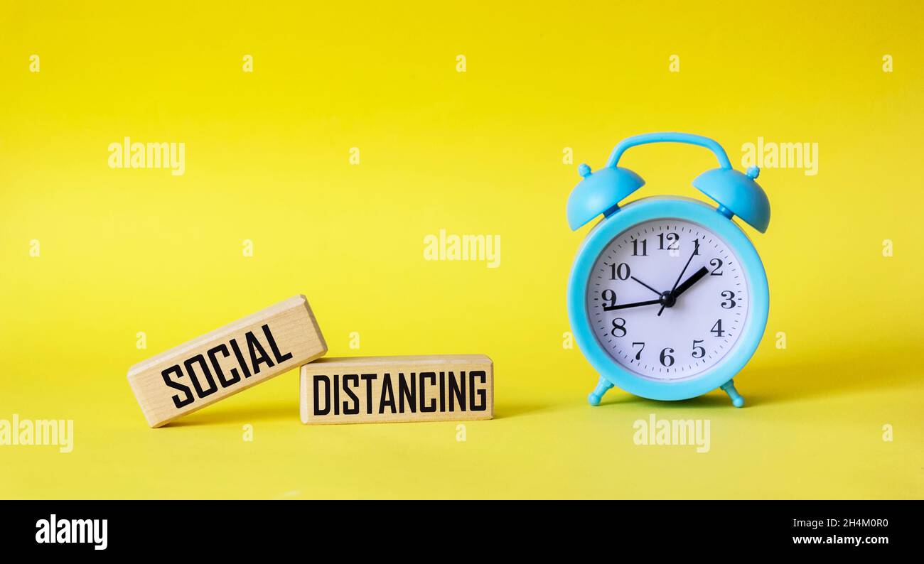 SOCIAL DISTANCE text on wooden block and yellow background with clock ...