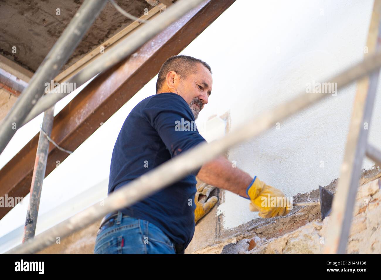 Construction worker on a ladder fixing a wall Stock Photo - Alamy
