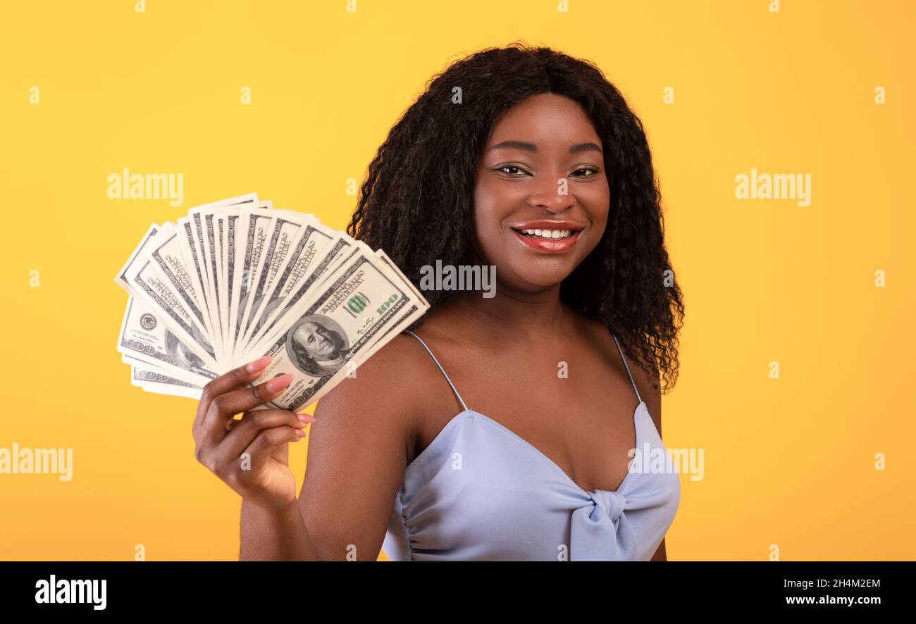 Confident African American woman holding fan of money and smiling at ...