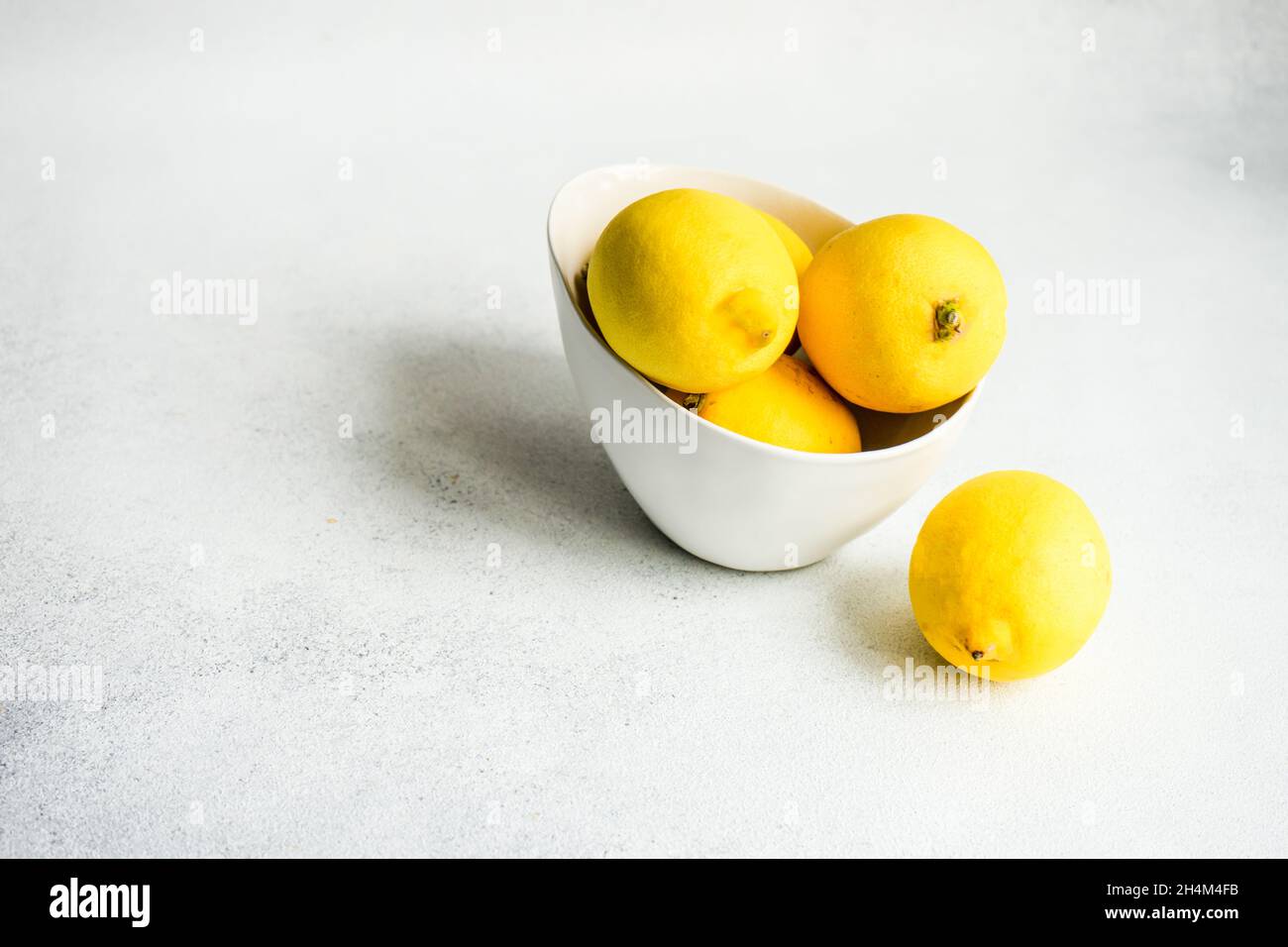 Organic raw and ripe lemon fruits in a bowl on white concrete ...