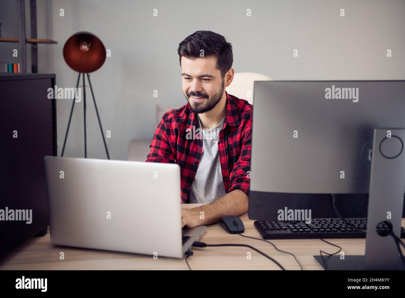 Photo of happy cheerful young man look write laptop sit desk programmer ...