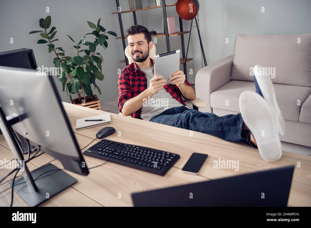 Full size photo of happy young cheerful man sit desk hold tablet look ...