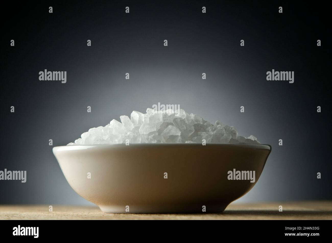 Salt crystals in small white bowl on timber table with grey spotlight ...