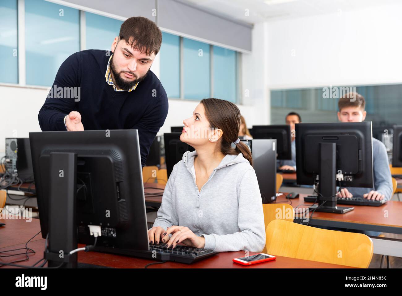 Male trainer helping young female student in computer class Stock Photo ...