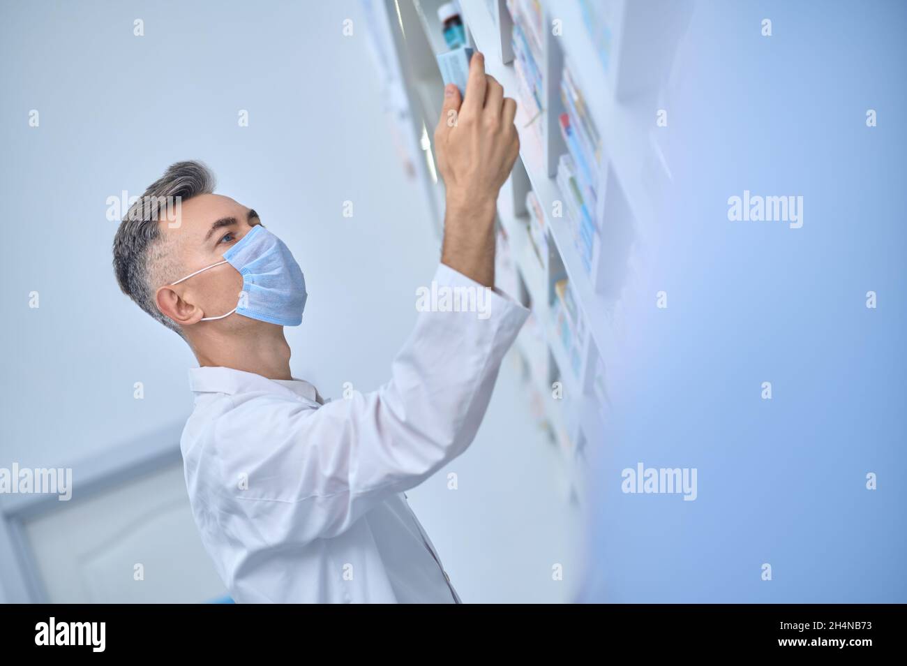 Pharmacist in protective mask considering medication with interest ...