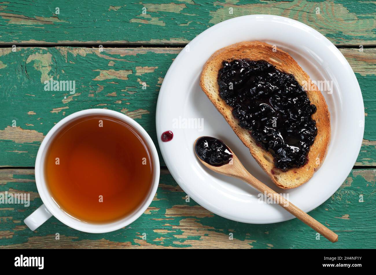 Cup of tea and toasted bread with blueberry jam in plate on old green ...