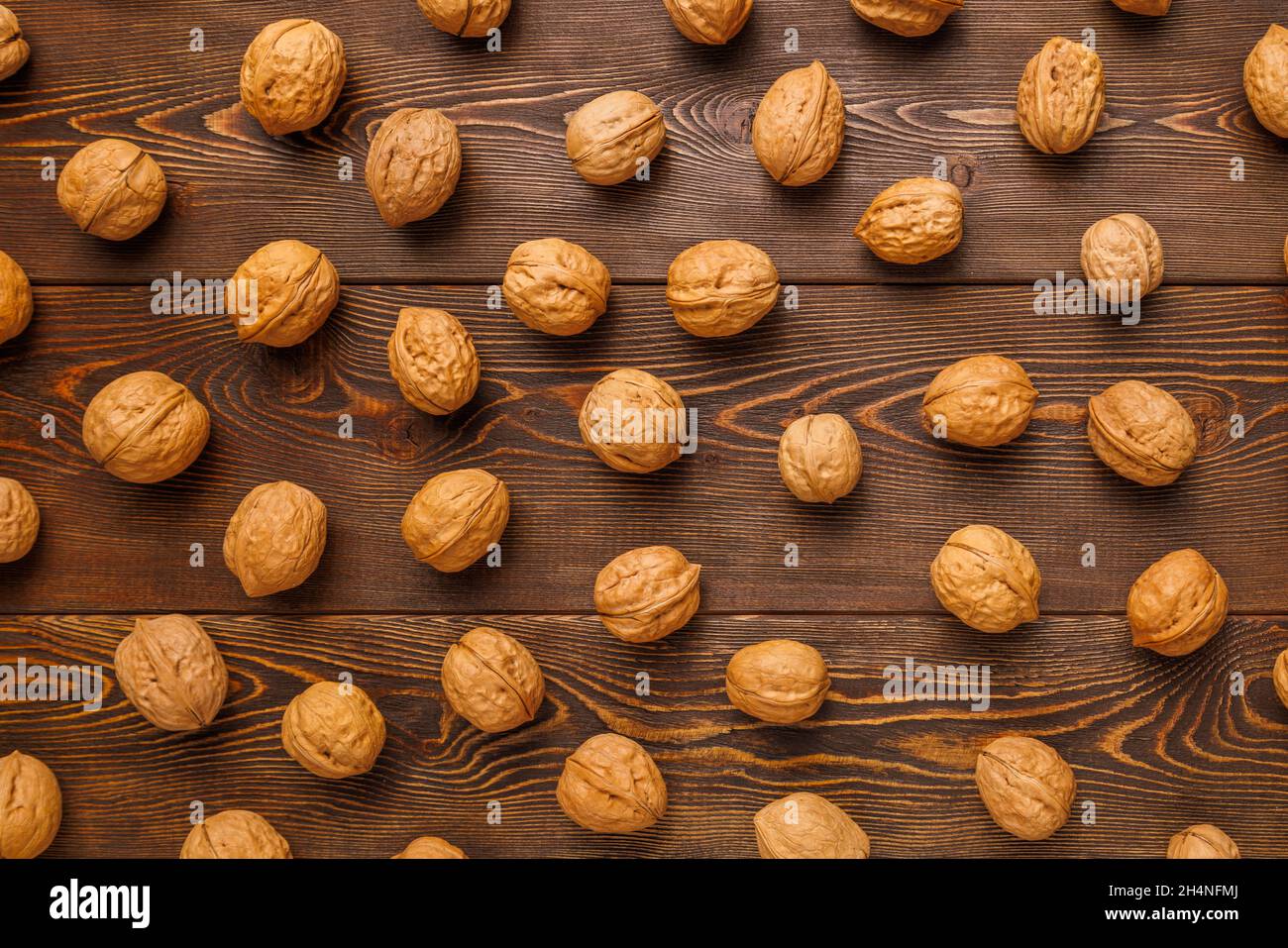 many walnuts with shells evenly spread out on brown wooden surface ...