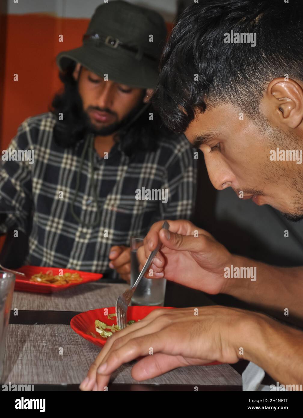 Two young guys eating noodles in the cafe. Two male friends having fast ...
