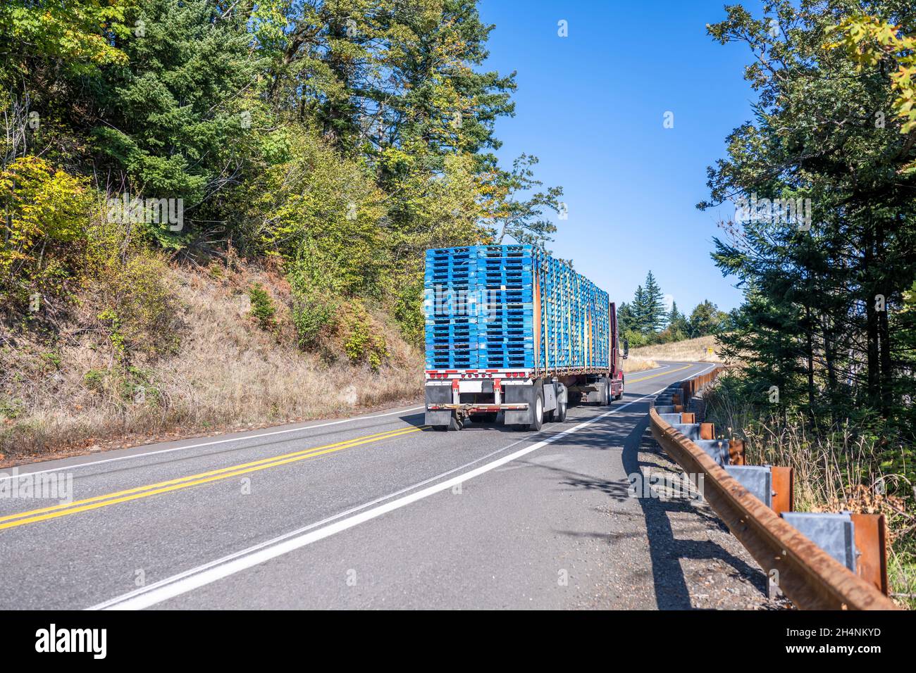 Powerful red big rig classic semi truck transporting fastened stacked ...