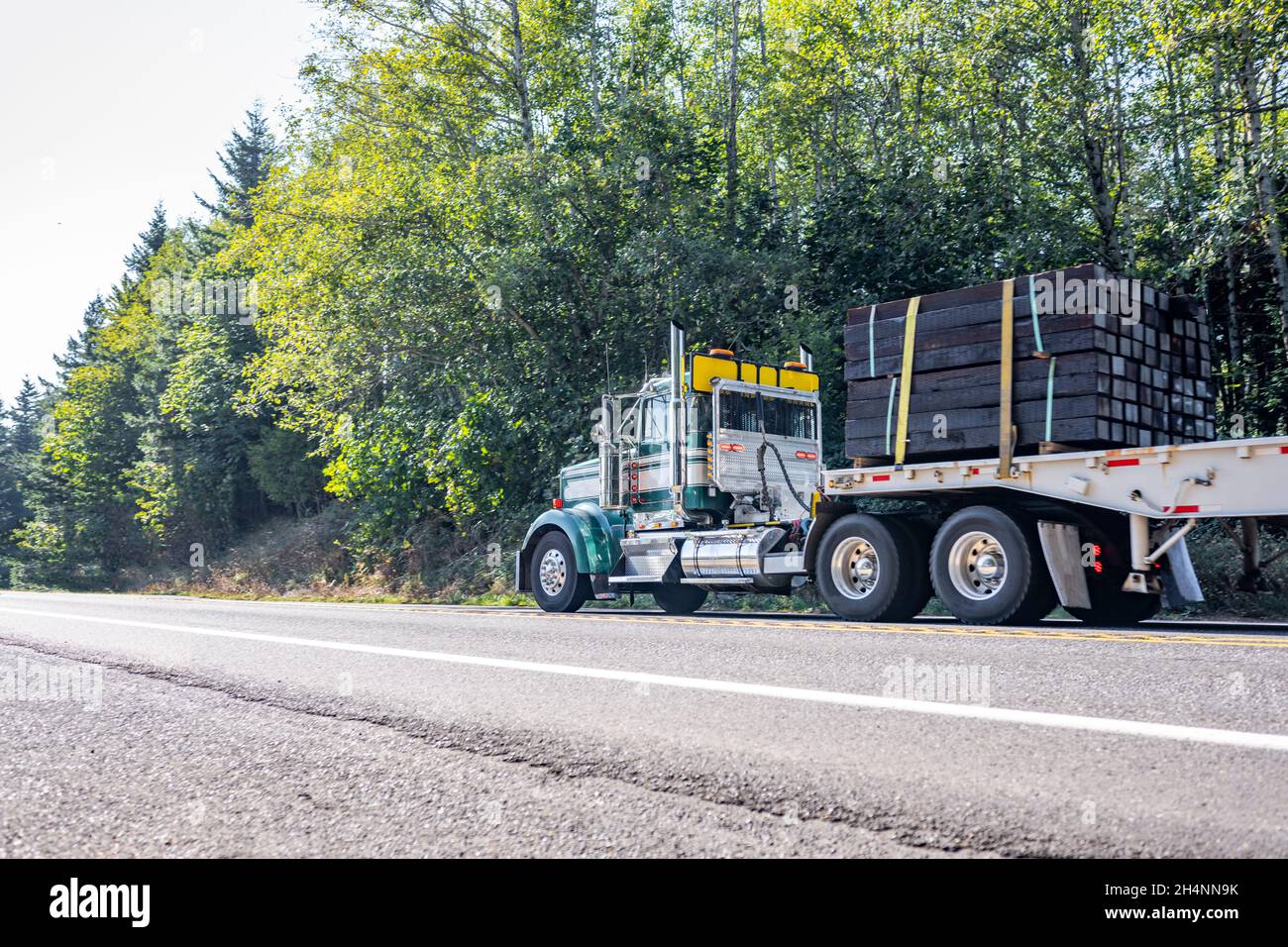 Powerful green big rig classic semi truck transporting fixed by slings ...