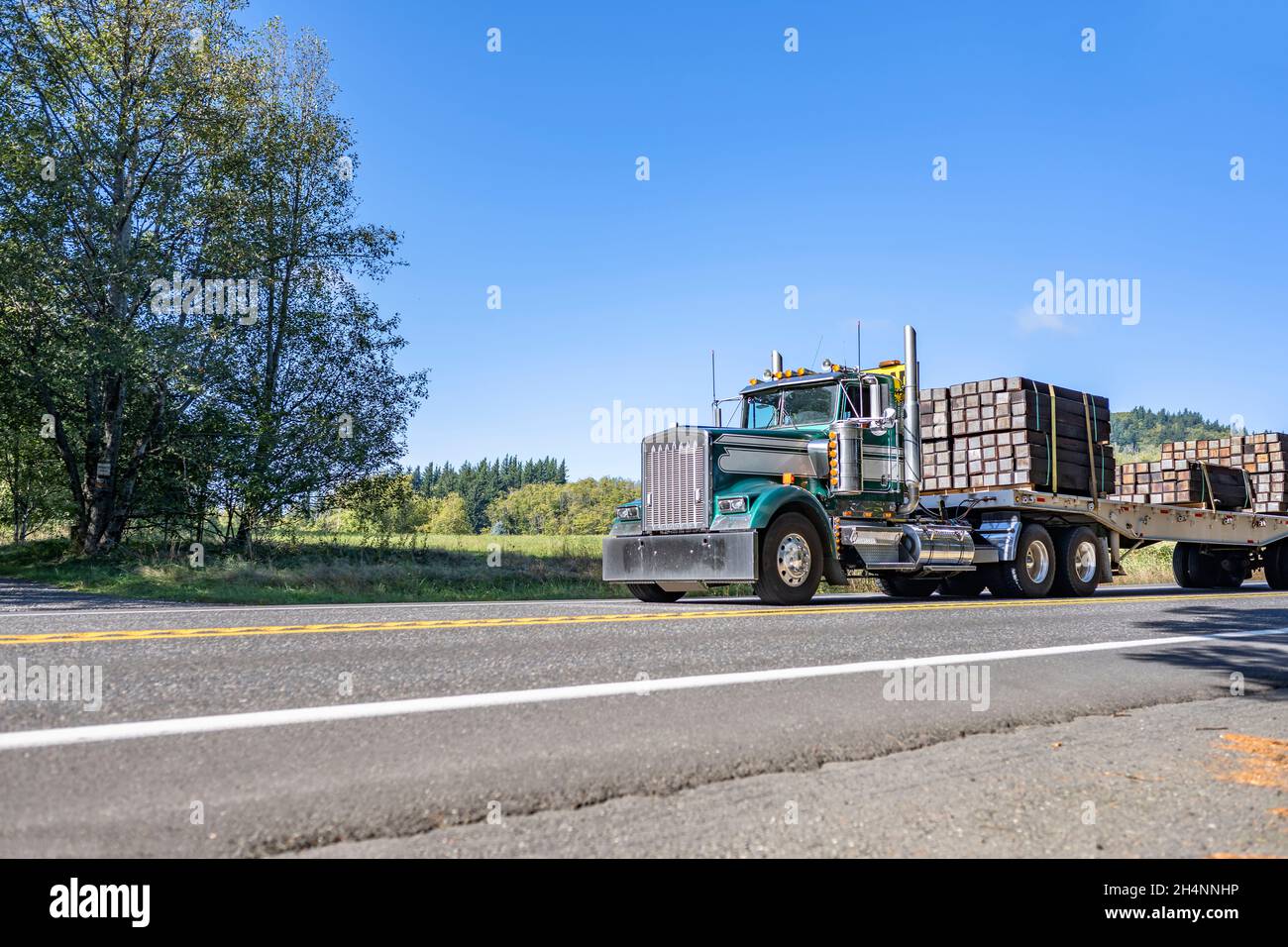 Powerful green big rig classic semi truck transporting fixed by slings ...