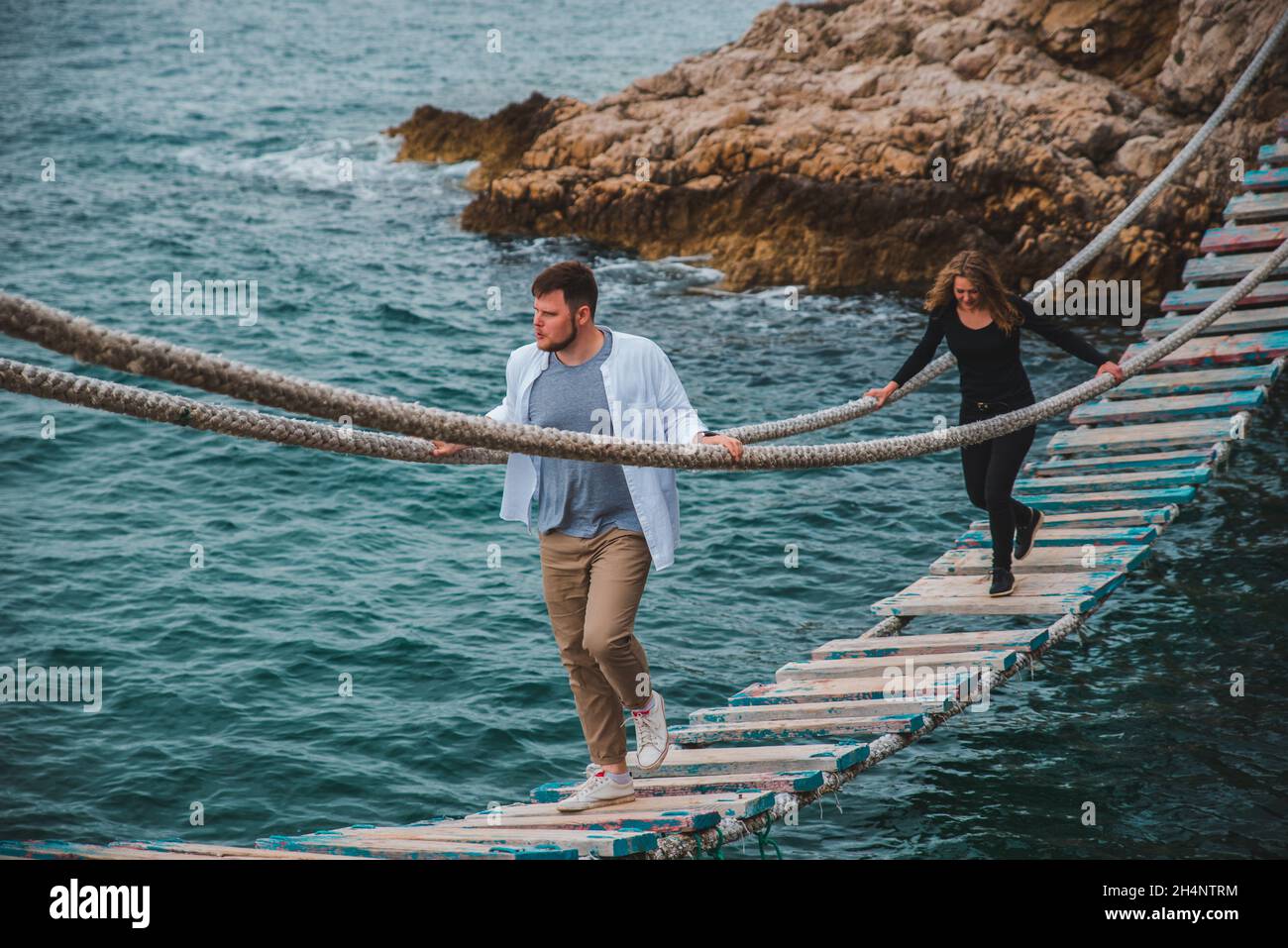 couple woman with man walking by shaky suspension bridge crossing sea ...