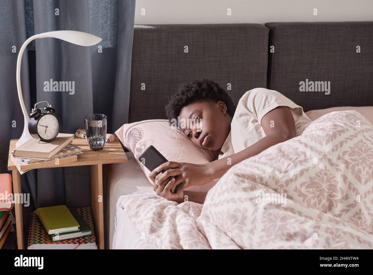 African young woman lying on the bed and using her mobile phone before ...