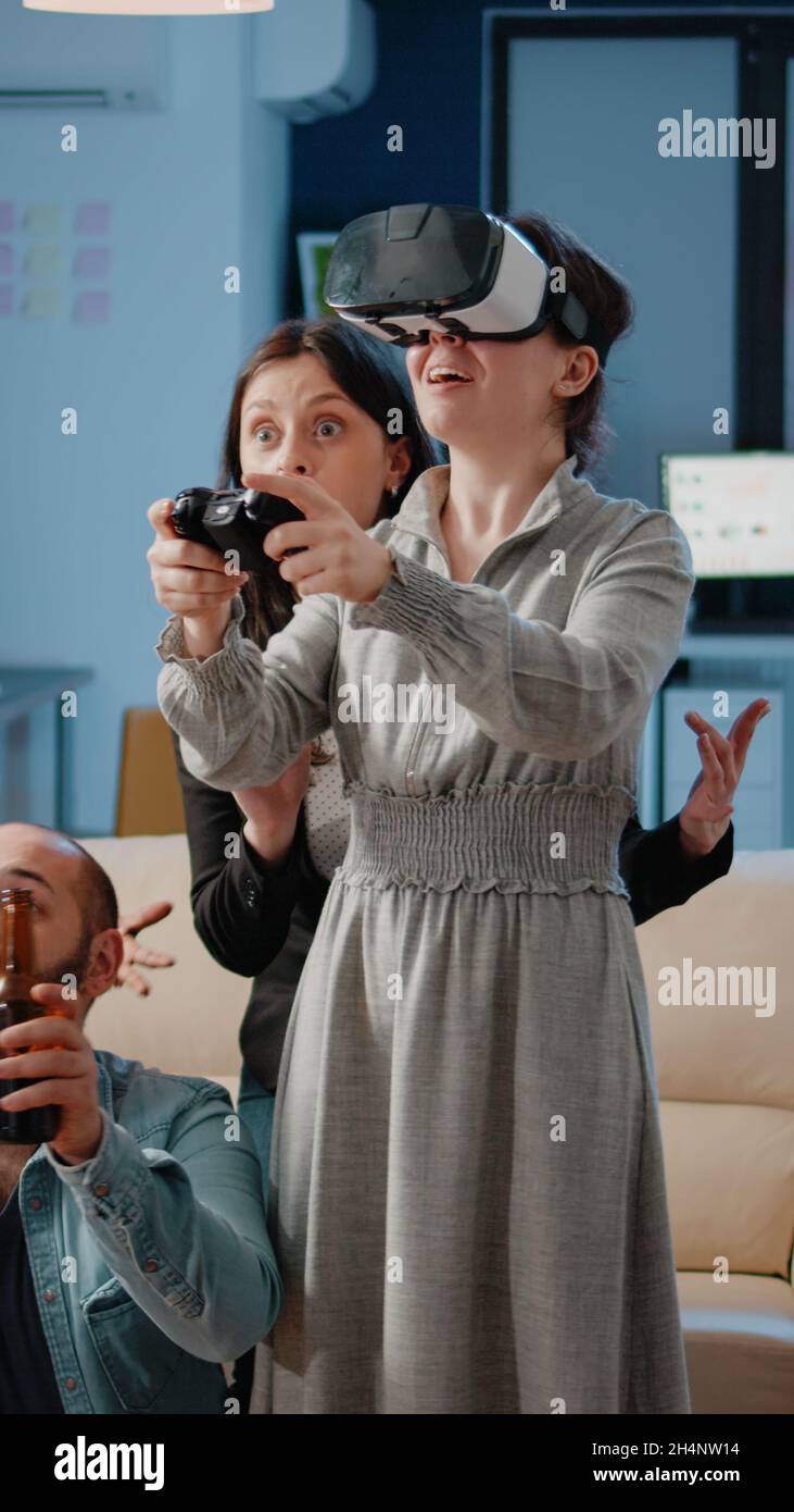 Woman using joystick and vr glasses while workmates cheering after work ...