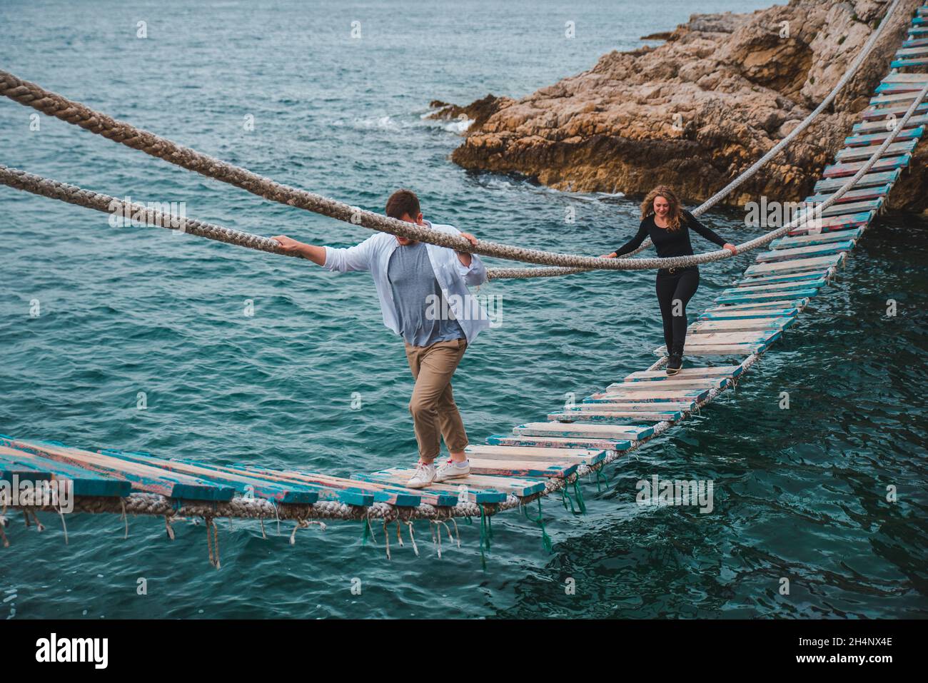 couple woman with man walking by shaky suspension bridge crossing sea ...
