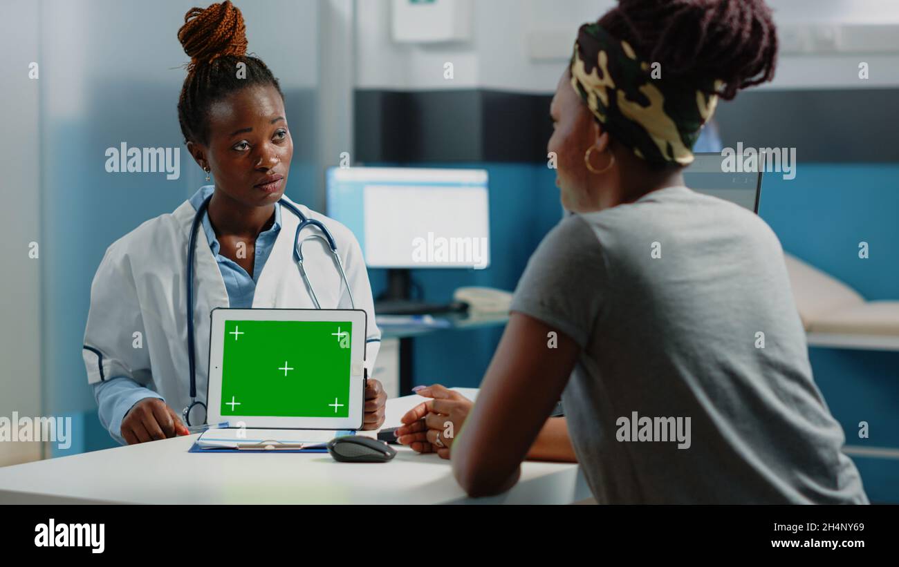 Black doctor showing tablet with horizontal green screen to patient at ...