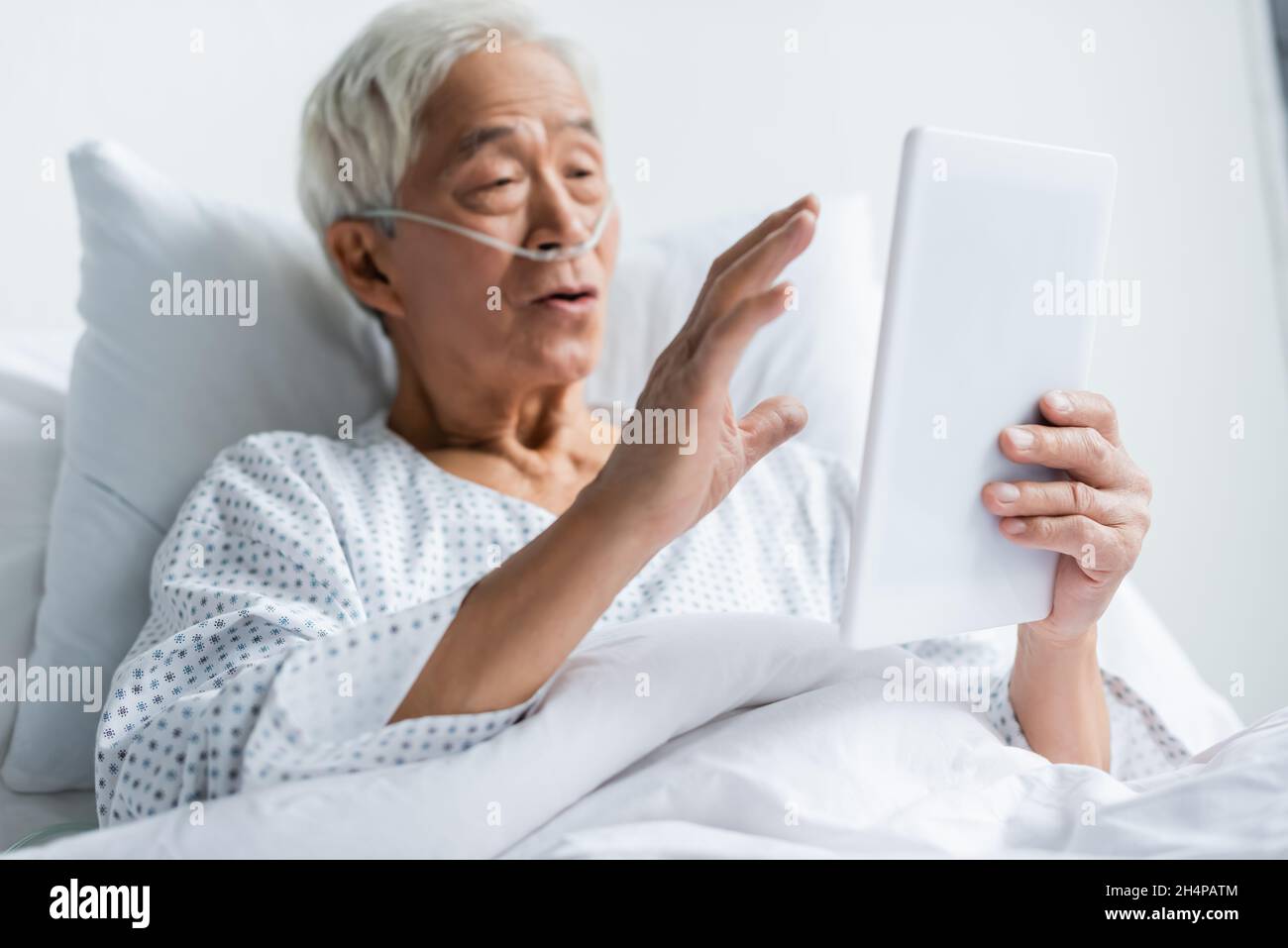 Digital tablet in hand of blurred asian patient with nasal cannula in ...