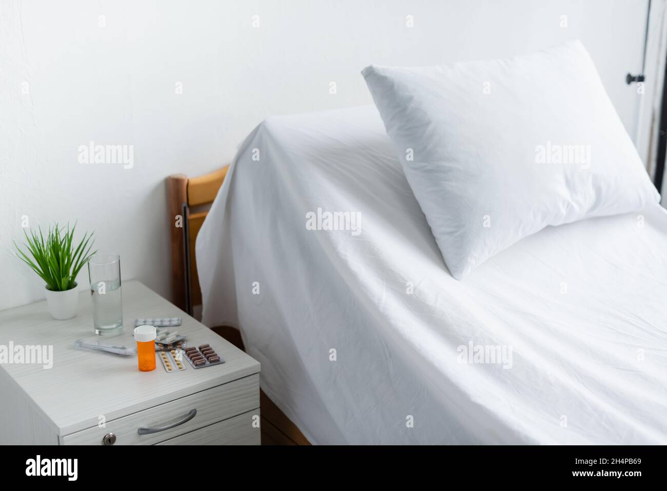 Pills and glass of water on bedside table near bed in hospital ward ...