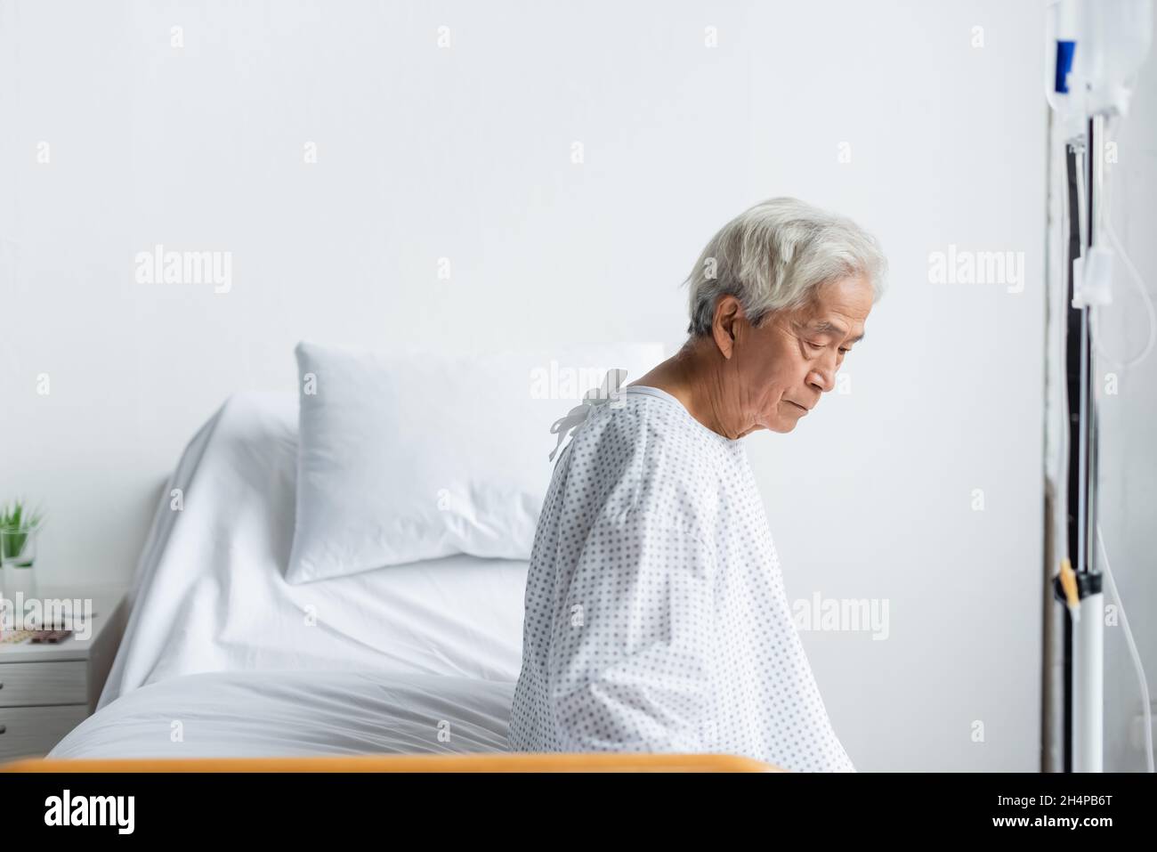 Sad asian patient sitting on bed near intravenous therapy in hospital ...