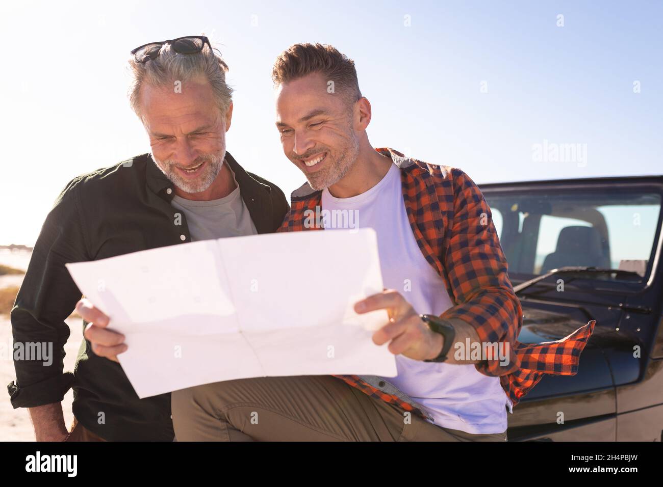 Happy caucasian gay male couple reading map, smiling by a car at ...