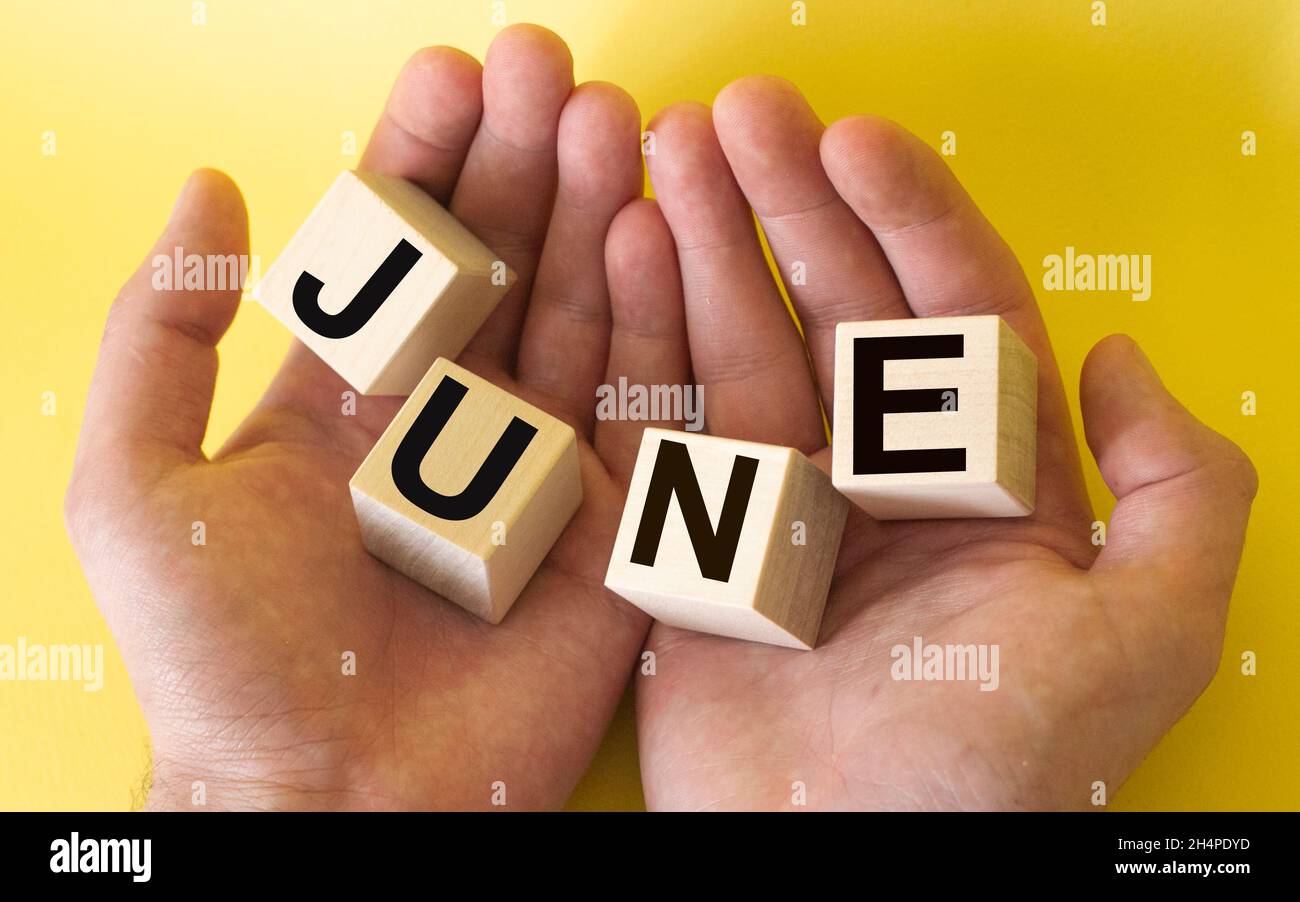 Men's hands are holding wooden blocks with the text June on a yellow ...
