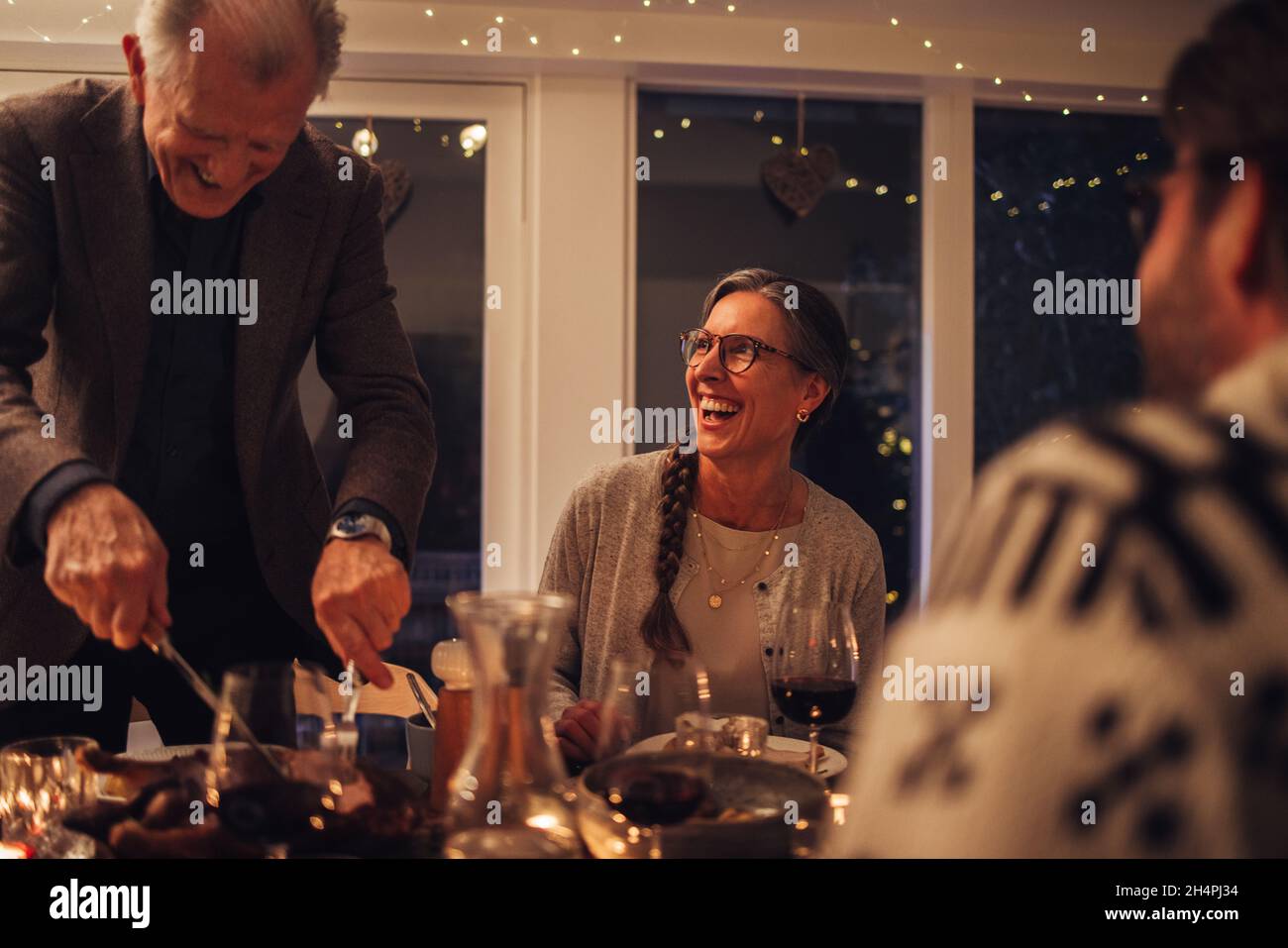 Senior man serving food to his family sitting at dinner table on ...