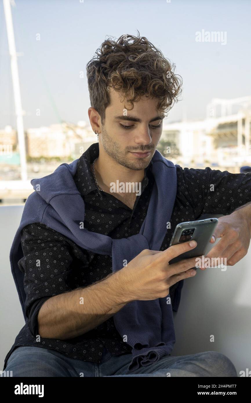 Young model poses sitting on a couch with a blue cardigan on his ...