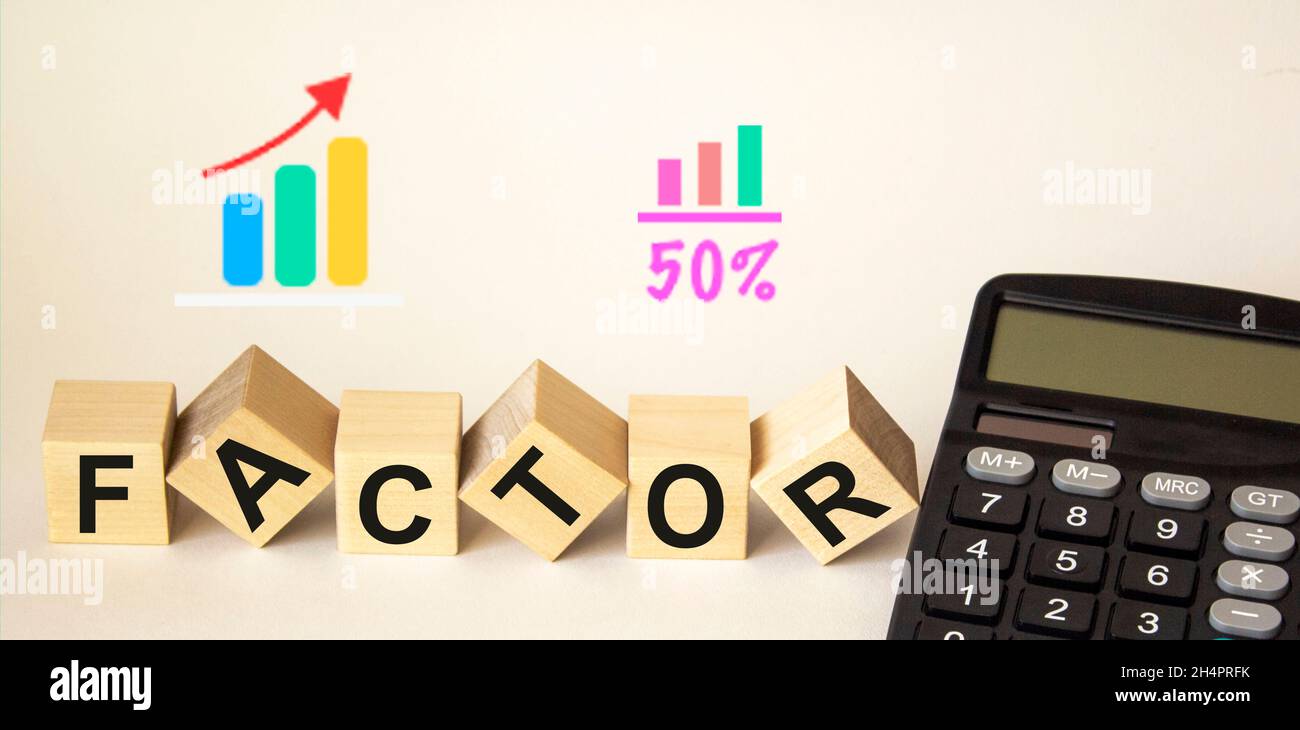 Word factor written in a wooden cube and a calculator with graphs on a ...